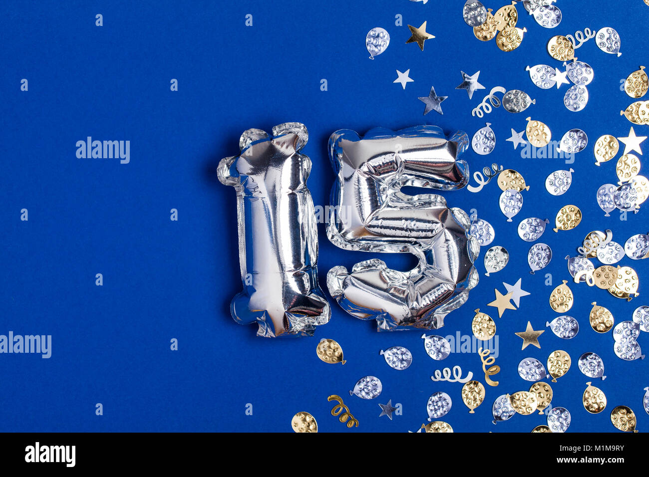 Silver foil number 15 balloon on a blue background with glitter ...