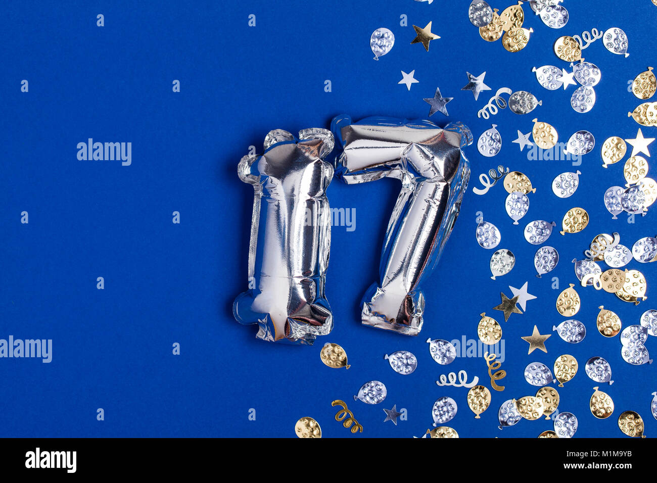Silver foil number 17 balloon on a blue background with glitter ...