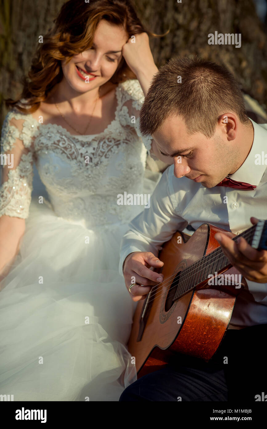 The beautiful bride with charming smile is enjoying the guitar play of ...