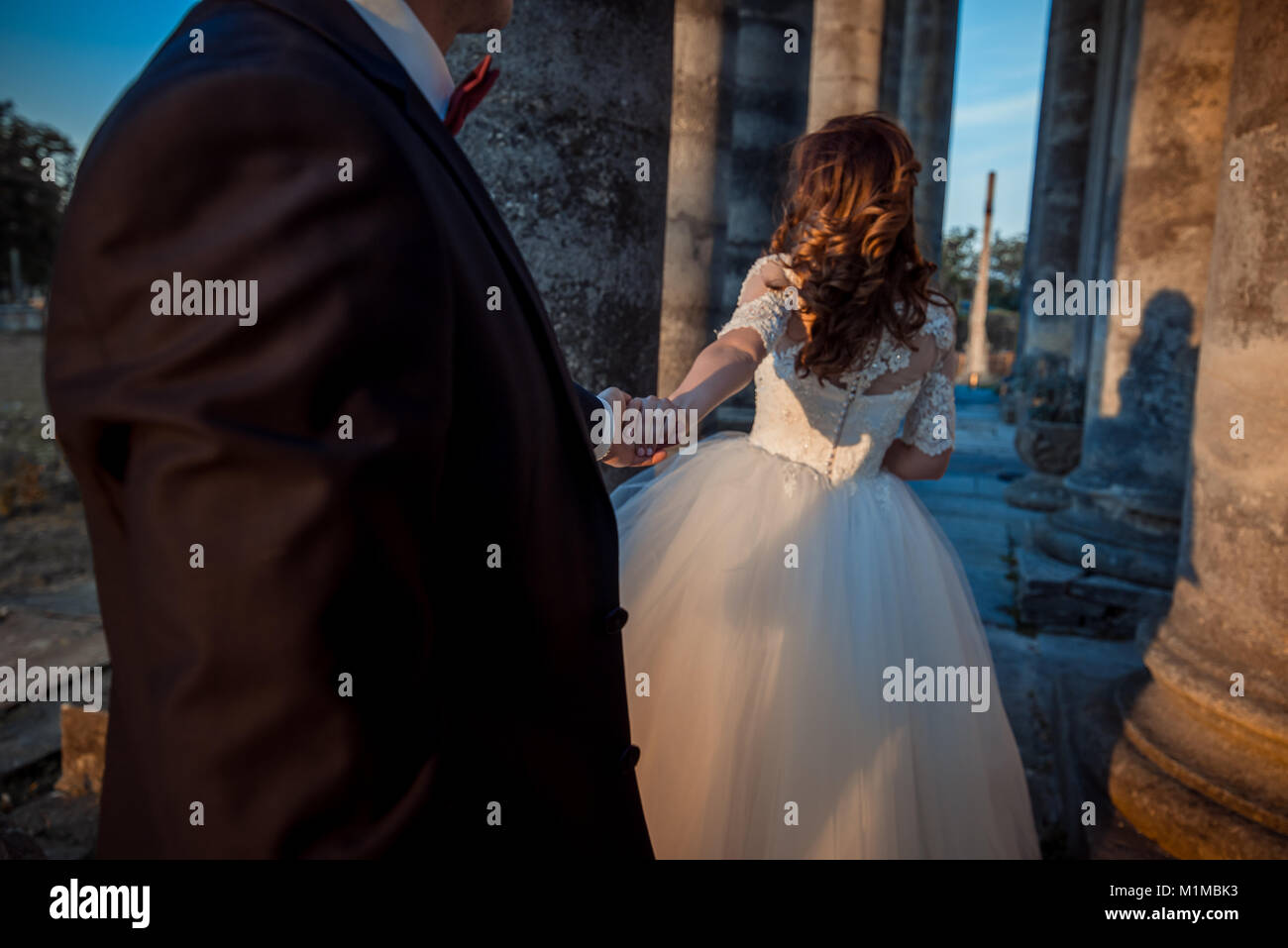 The bride with beautiful ginger curly hair is leading the groom by the ...