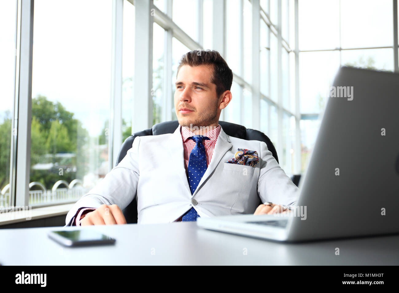 Portrait of young man sitting at his desk in the office Stock Photo - Alamy