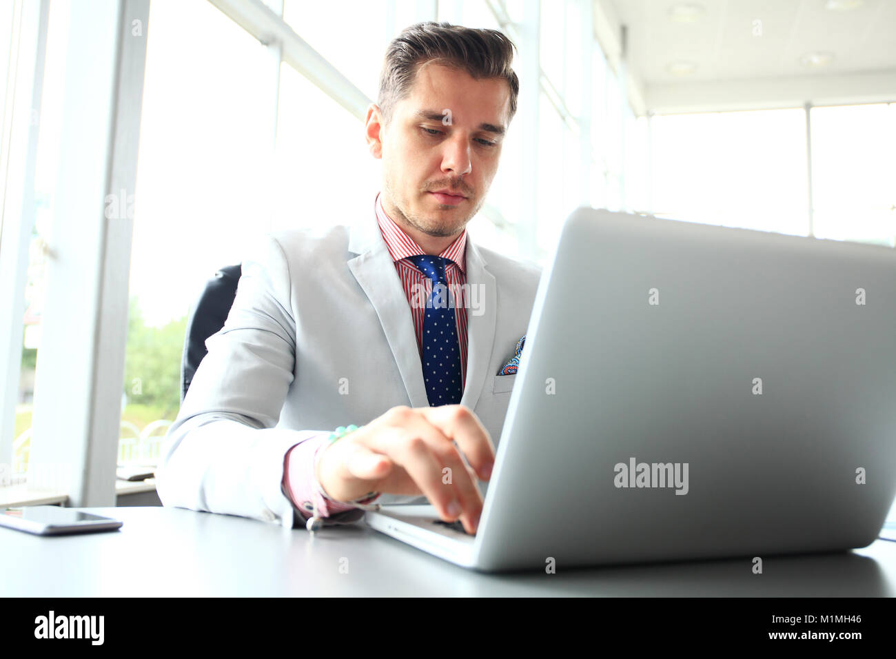 Portrait of young man sitting at his desk in the office Stock Photo - Alamy