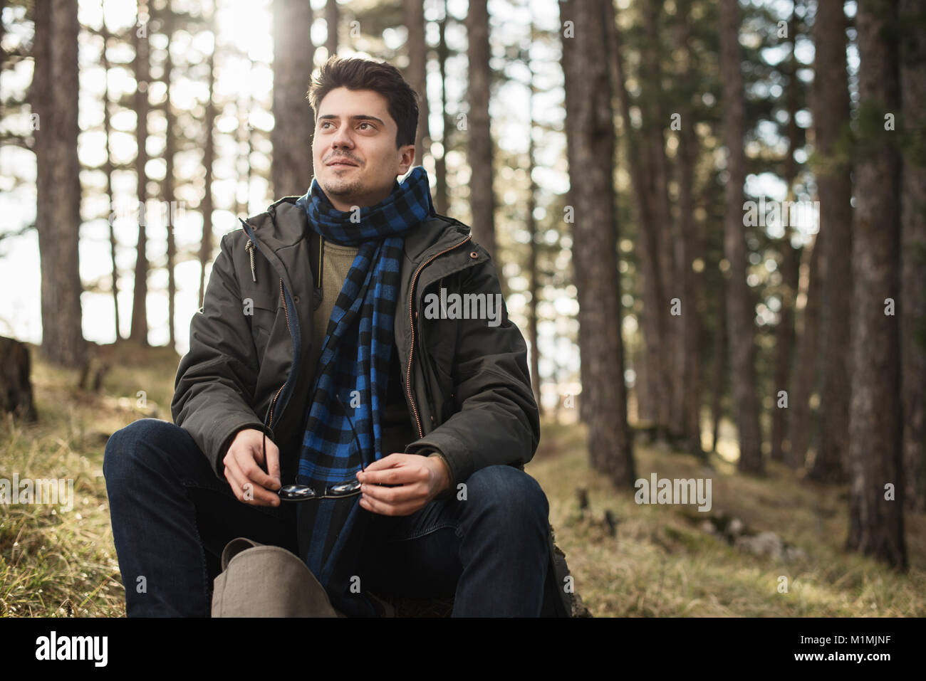 Man sitting in forest holding sunglasses Stock Photo - Alamy