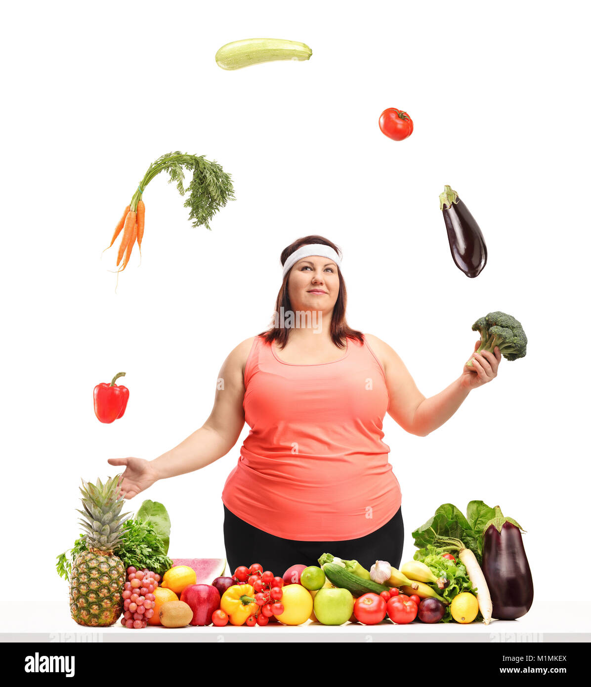 Overweight woman juggling vegetables behind a table with fruit and ...