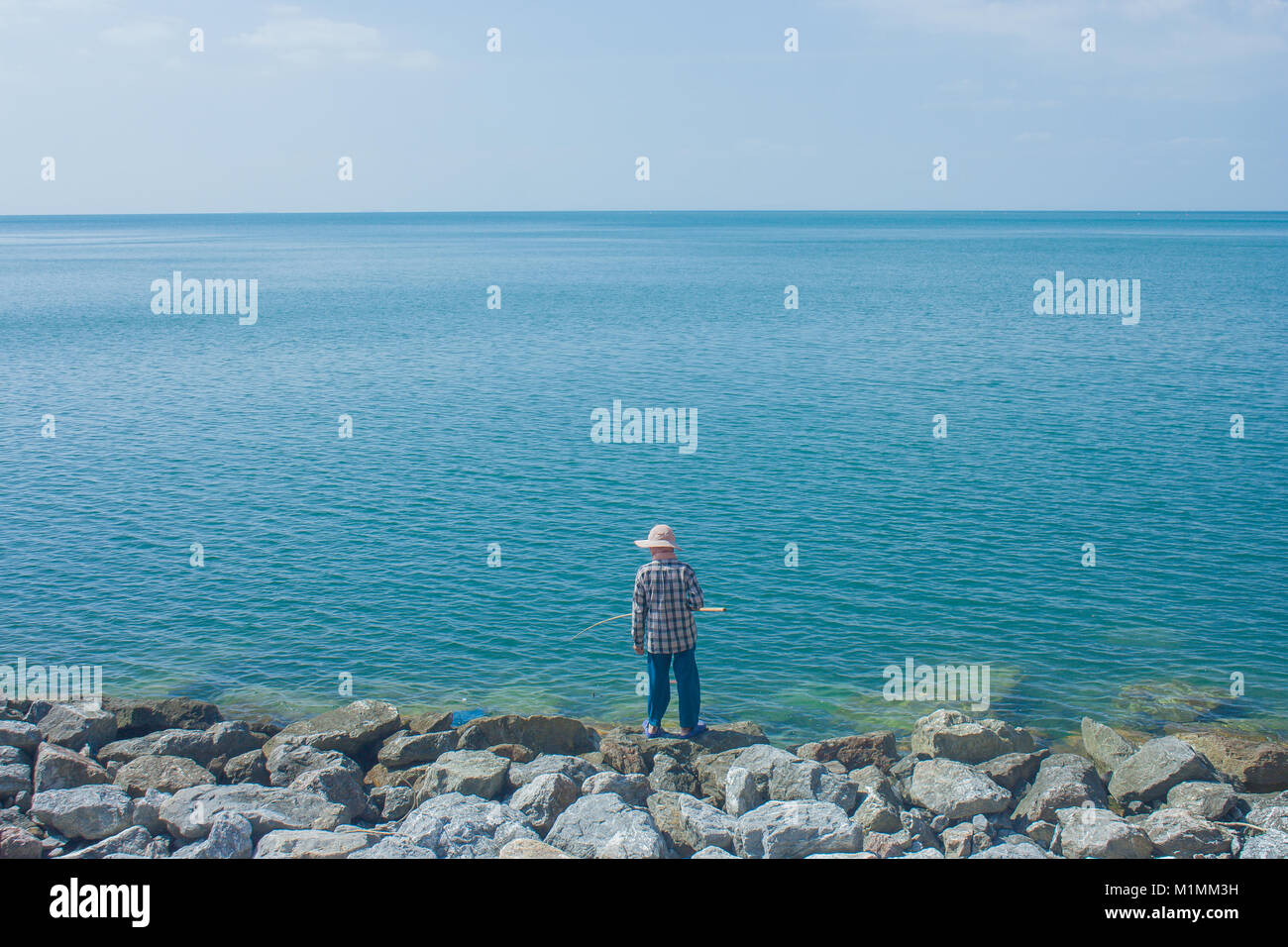 Fisherman standing on the shore and holding fishing rod in his hand ...