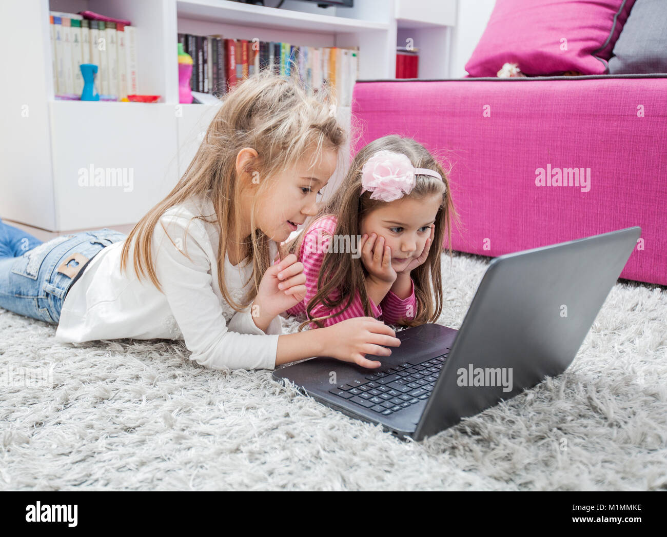 Two little girls working with laptop at home, children using computer ...