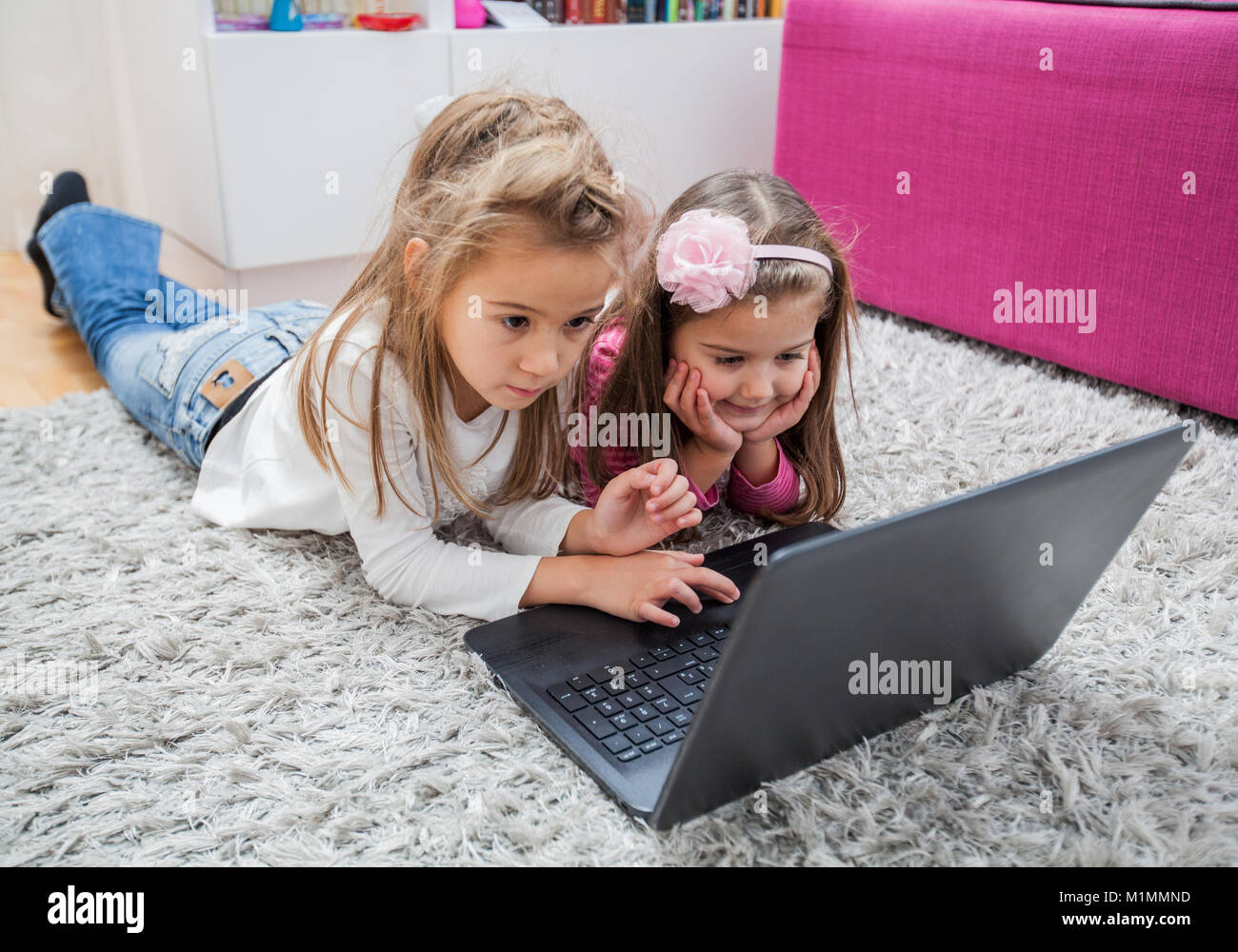 Two little girls working with laptop at home, children using computer ...