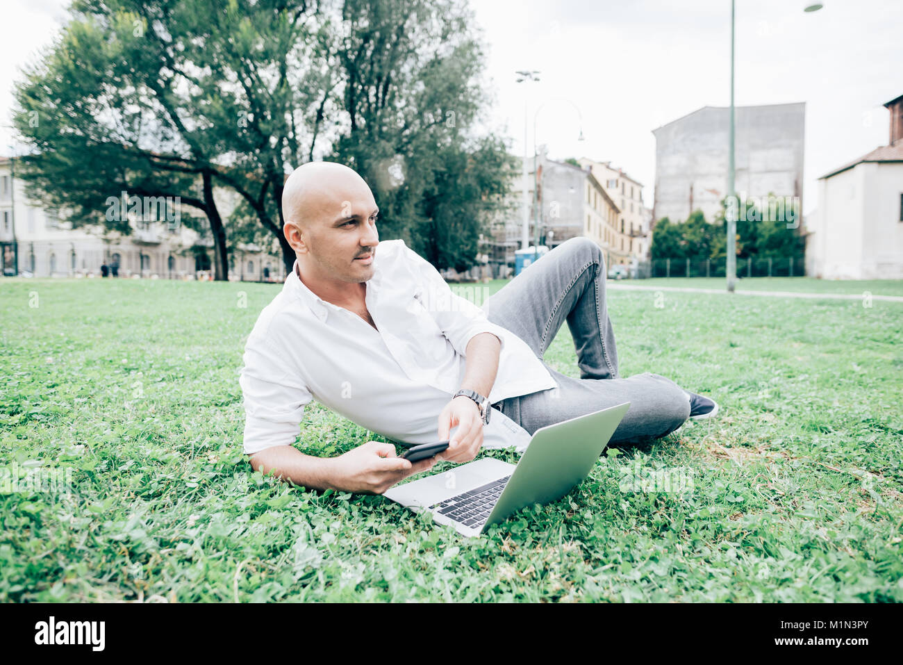 Young contemporary businessman remote working lying down outdoor in a ...