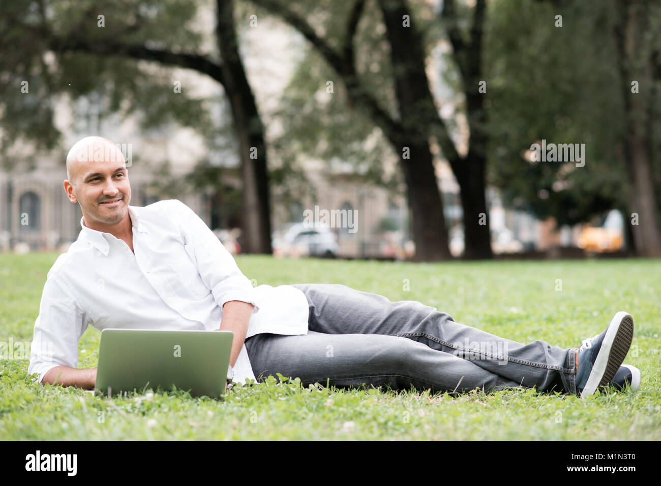 Young contemporary businessman remote working lying down outdoor in a ...