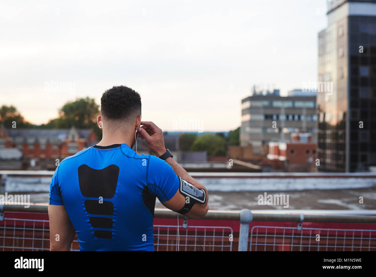 Male runner adjusting earphones in urban setting, back view Stock Photo ...