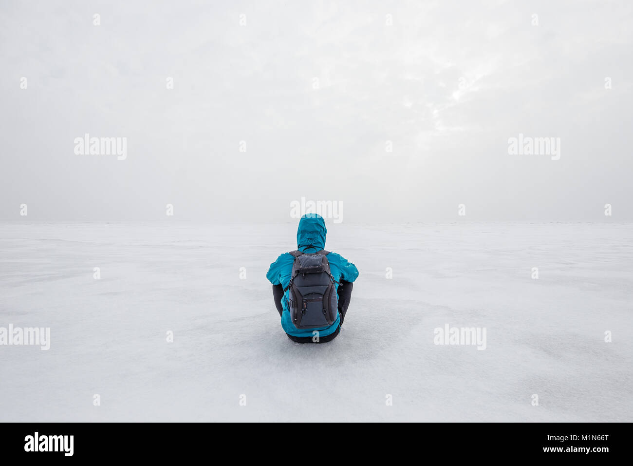 Man with backpack sitting alone on the lake ice and staring forward ...