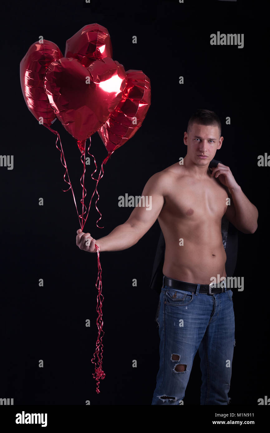 muscular young man holding a heart shaped balloon against black ...