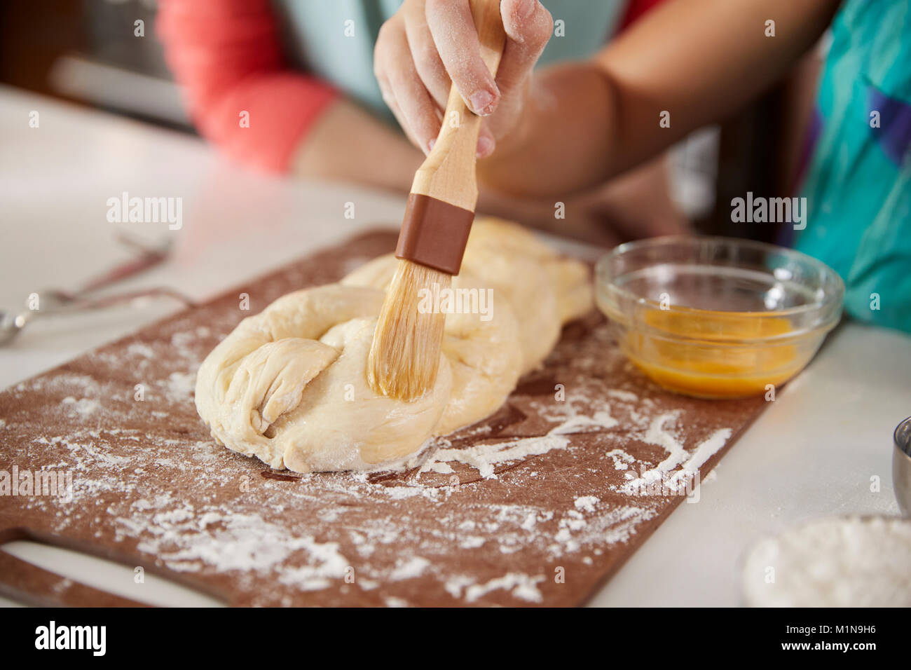 Jewish girl glazing plaited challah dough with mum, close up Stock ...