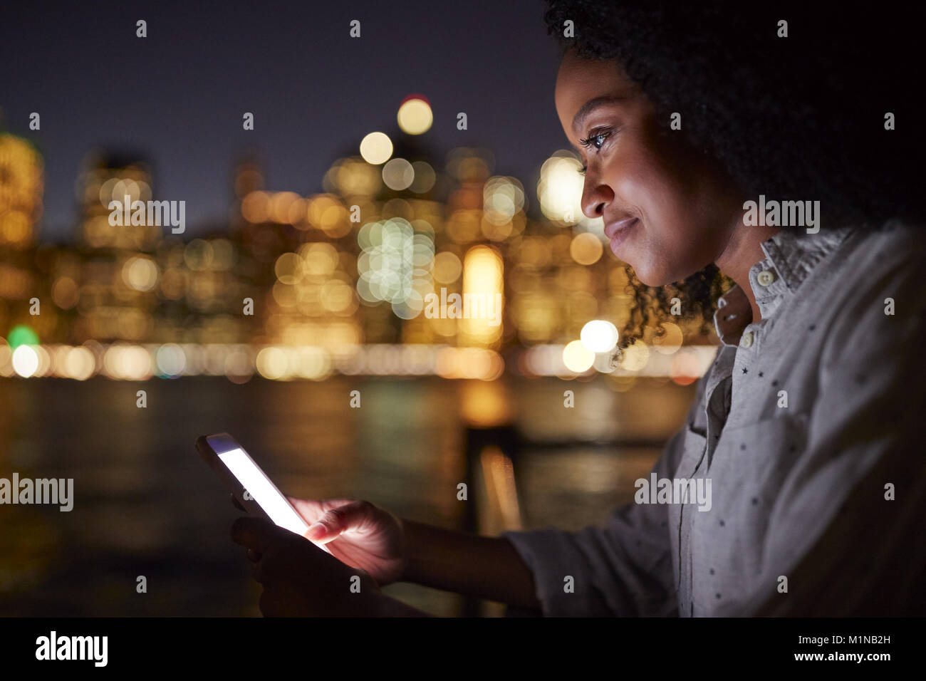 Woman Uses Mobile Phone At Night With City Skyline In Background Stock ...