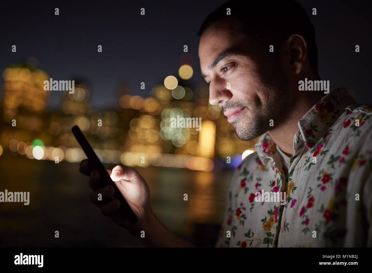 Man Using Mobile Phone At Night With City Skyline In Background Stock ...