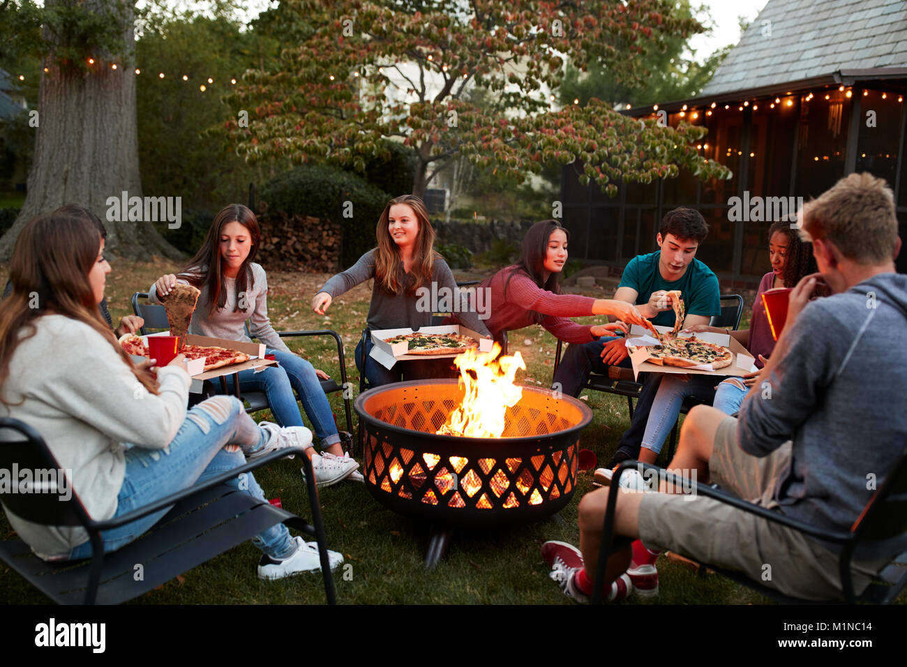Teenage friends sit round a fire pit eating take-away pizzas Stock ...