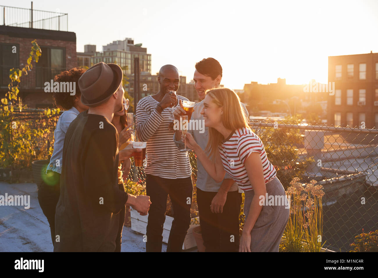 Friends stand talking at rooftop party, backlit by sunlight Stock Photo ...