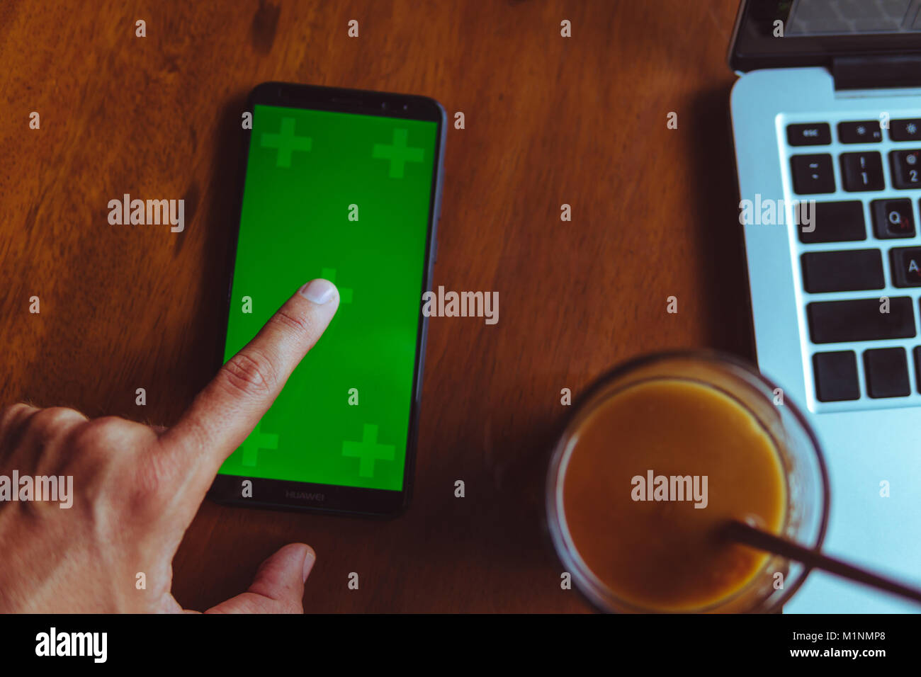 Finger of man tap on smartphone with green screen near. Coffee, laptop ...