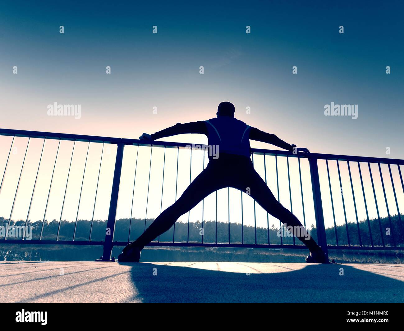 The runner in tall black leggings makes body stretching on bridge path ...