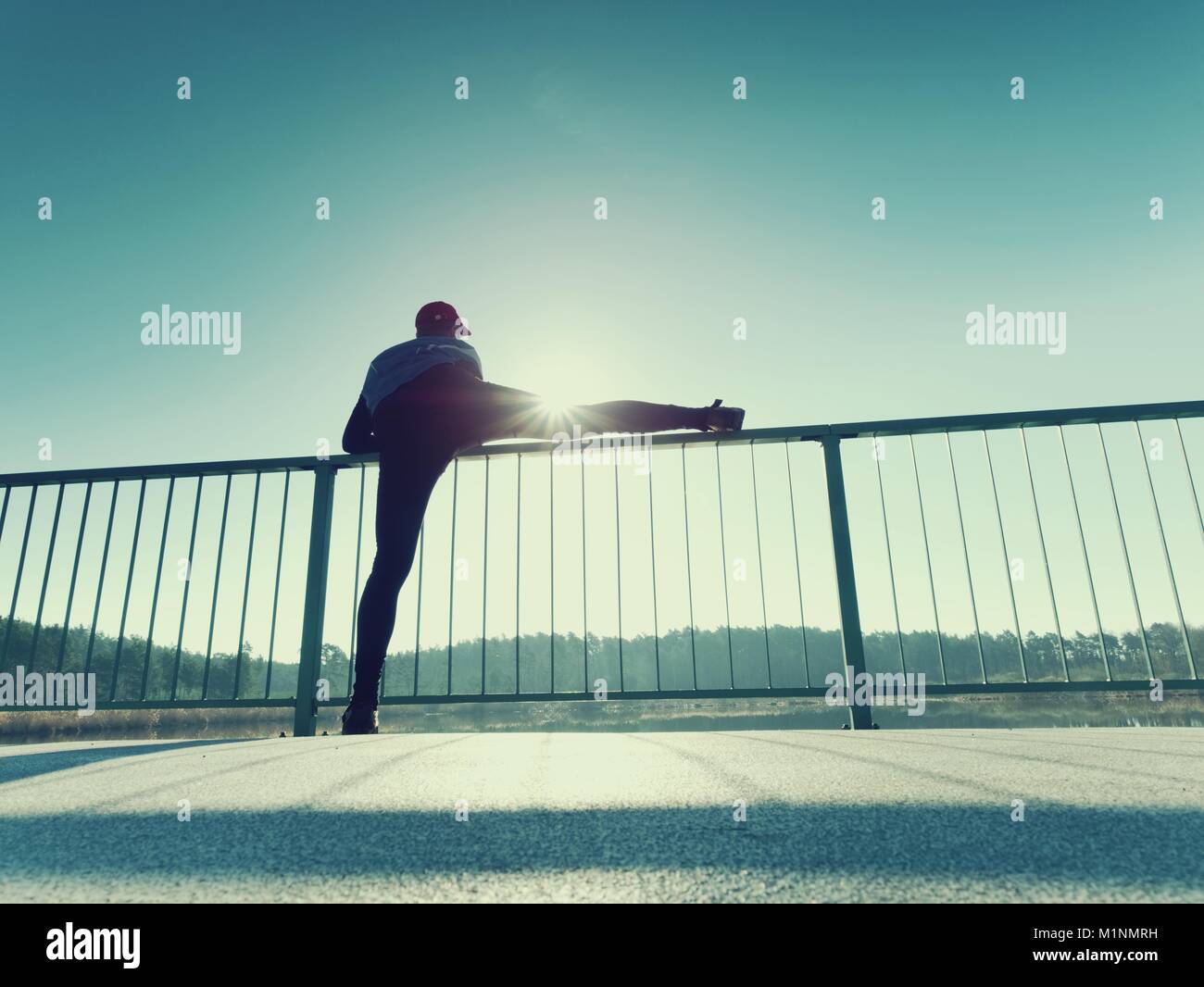 The runner in tall black leggings makes body stretching on bridge path ...