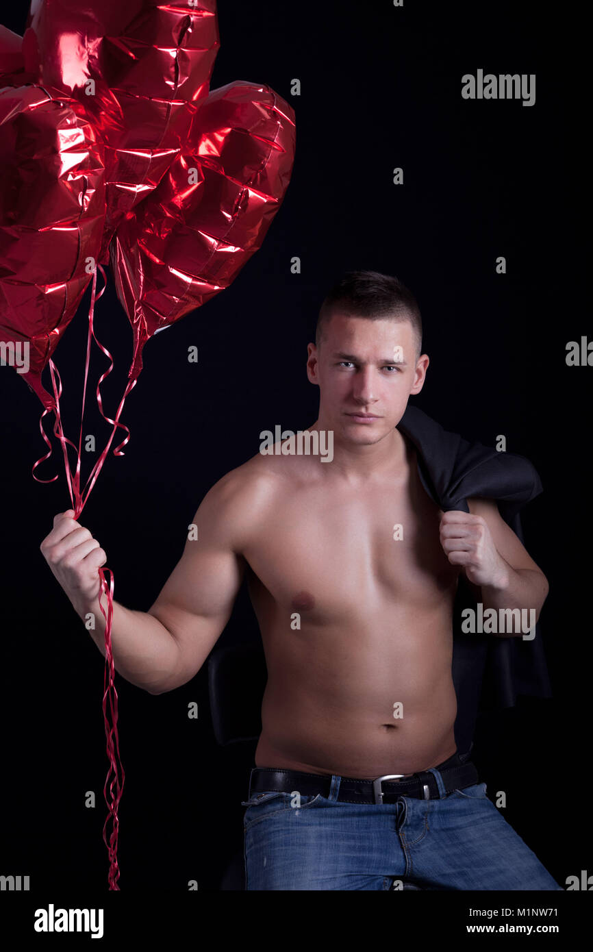 muscular young man holding a heart shaped balloon against black ...