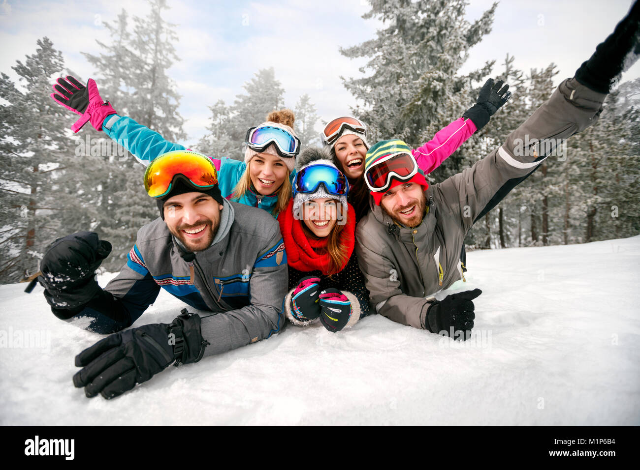 smiling friends on winter holidays – Happy skiers lying on snow and ...