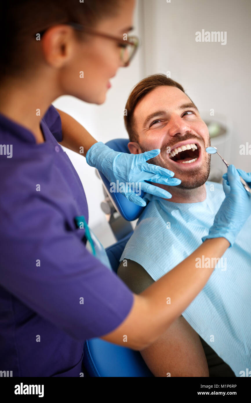 Female dentist with dental mirror looking patiens teeth in dental clinc ...