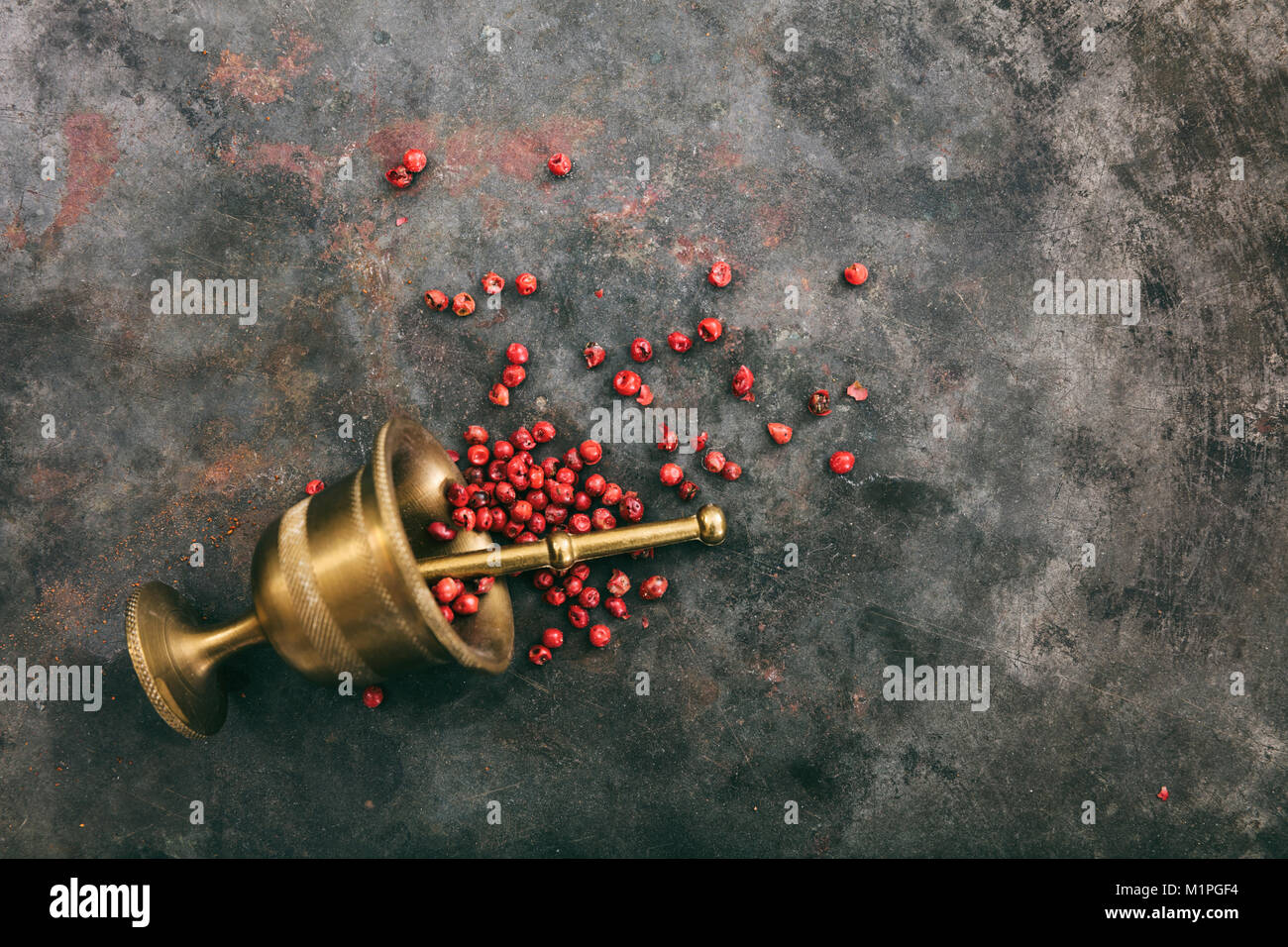 Pink pepper seeds and a brass mortar on metal rusty background, top ...