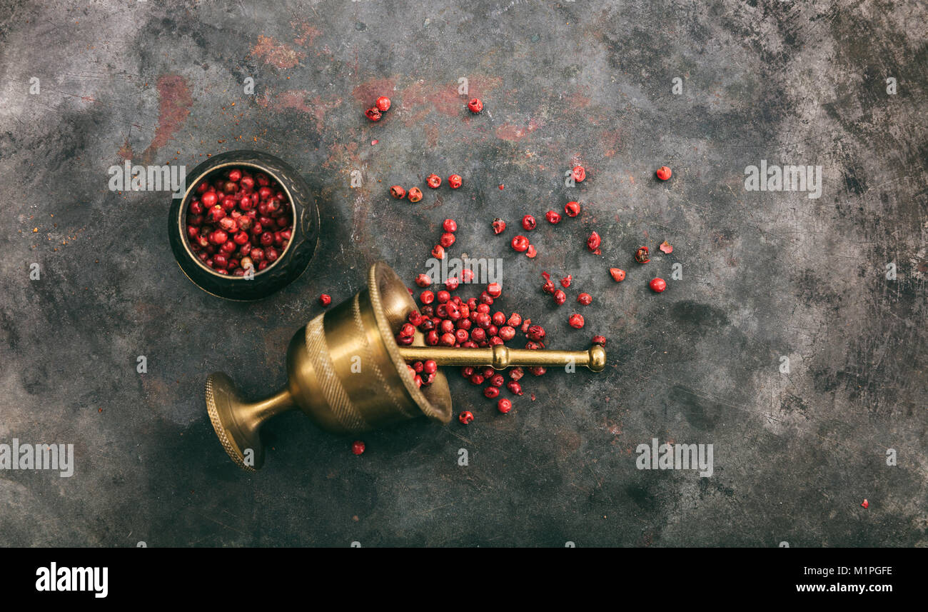 Pink pepper seeds and a brass mortar on metal rusty background, top ...