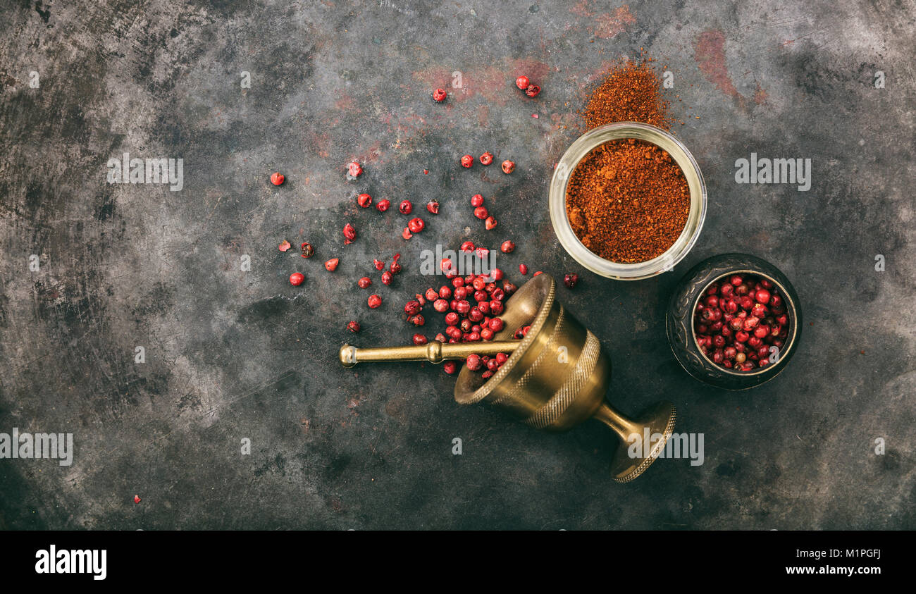 Pink pepper seeds and powder and a brass mortar on metal rusty ...