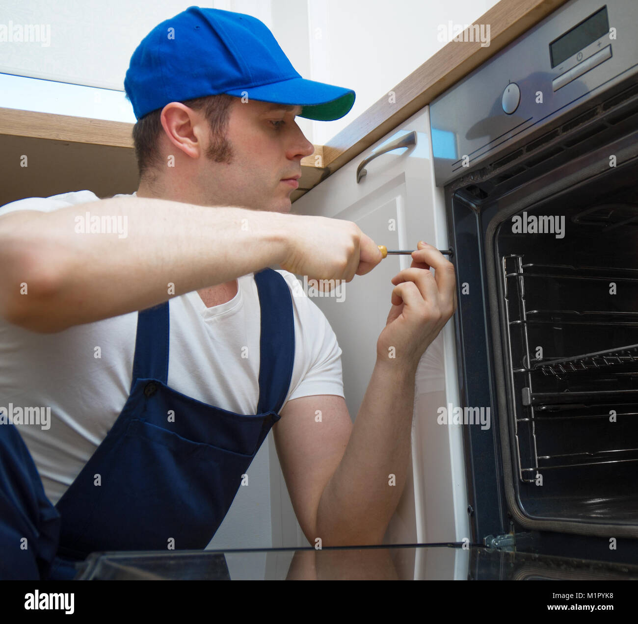 Professional handyman in overalls repairing domestic oven in the ...