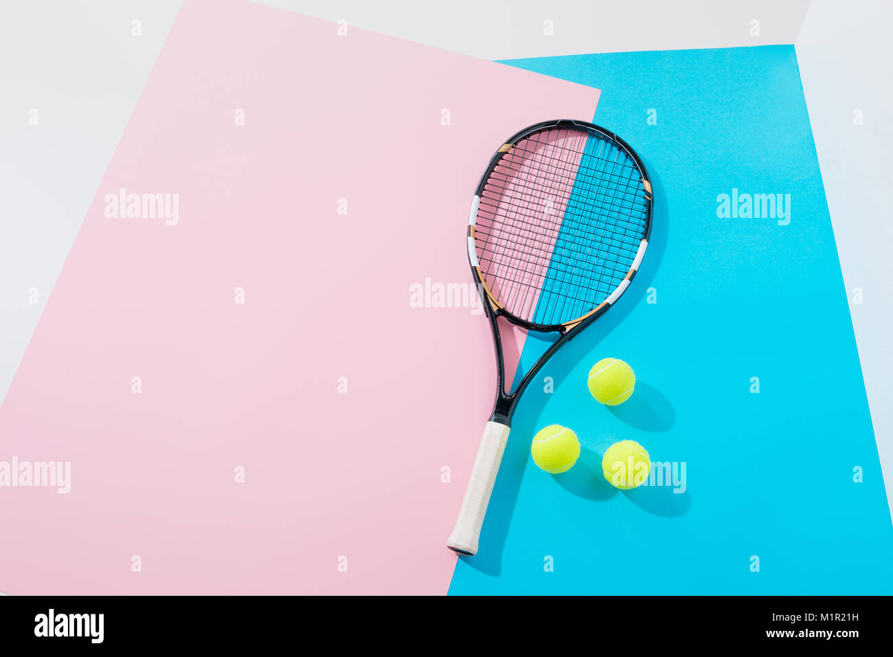 top view of tennis racket and yellow balls on blue and pink papers ...
