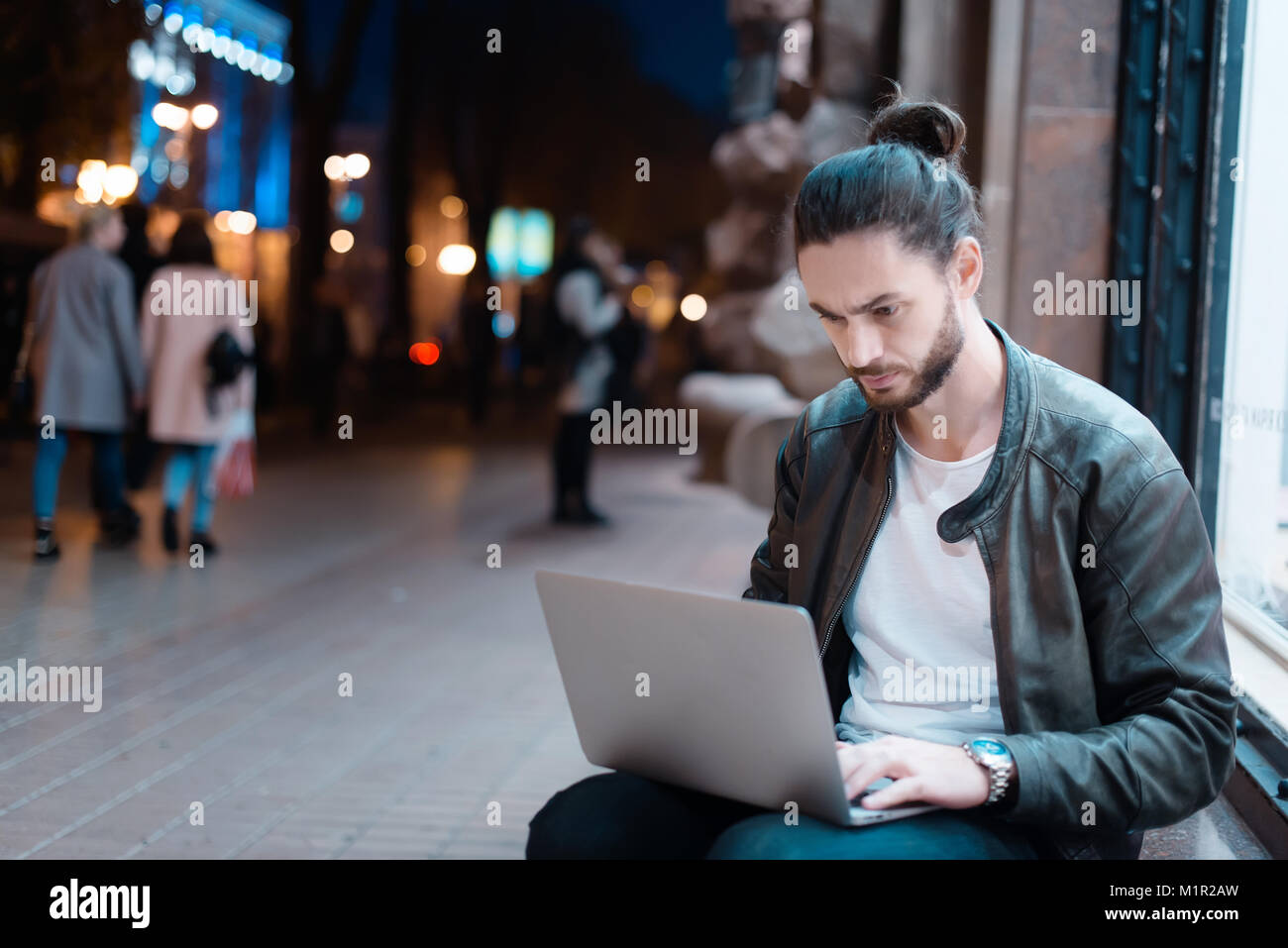A guy with a laptop in a night city. The tourist is sitting and using a ...