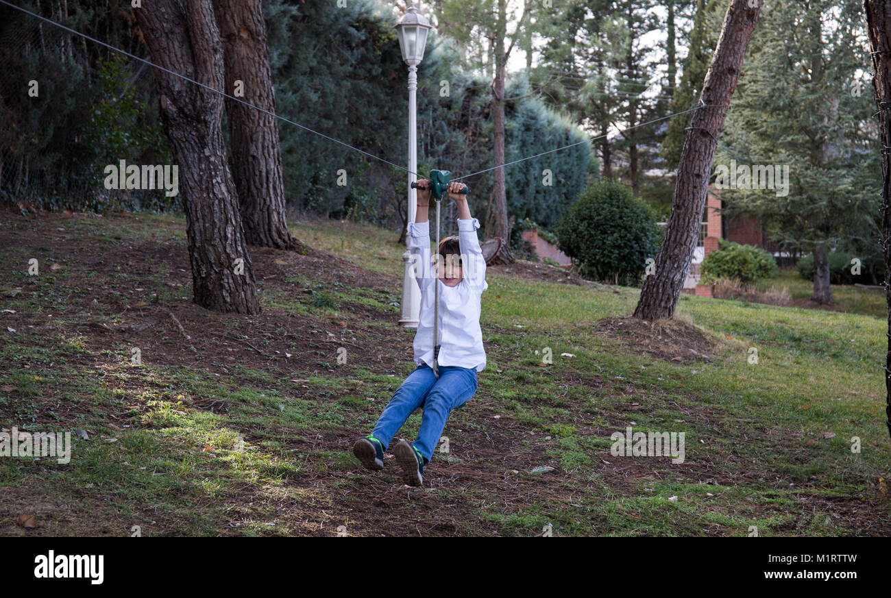 Child playing and sliding on a zip line between two trees in his garden ...