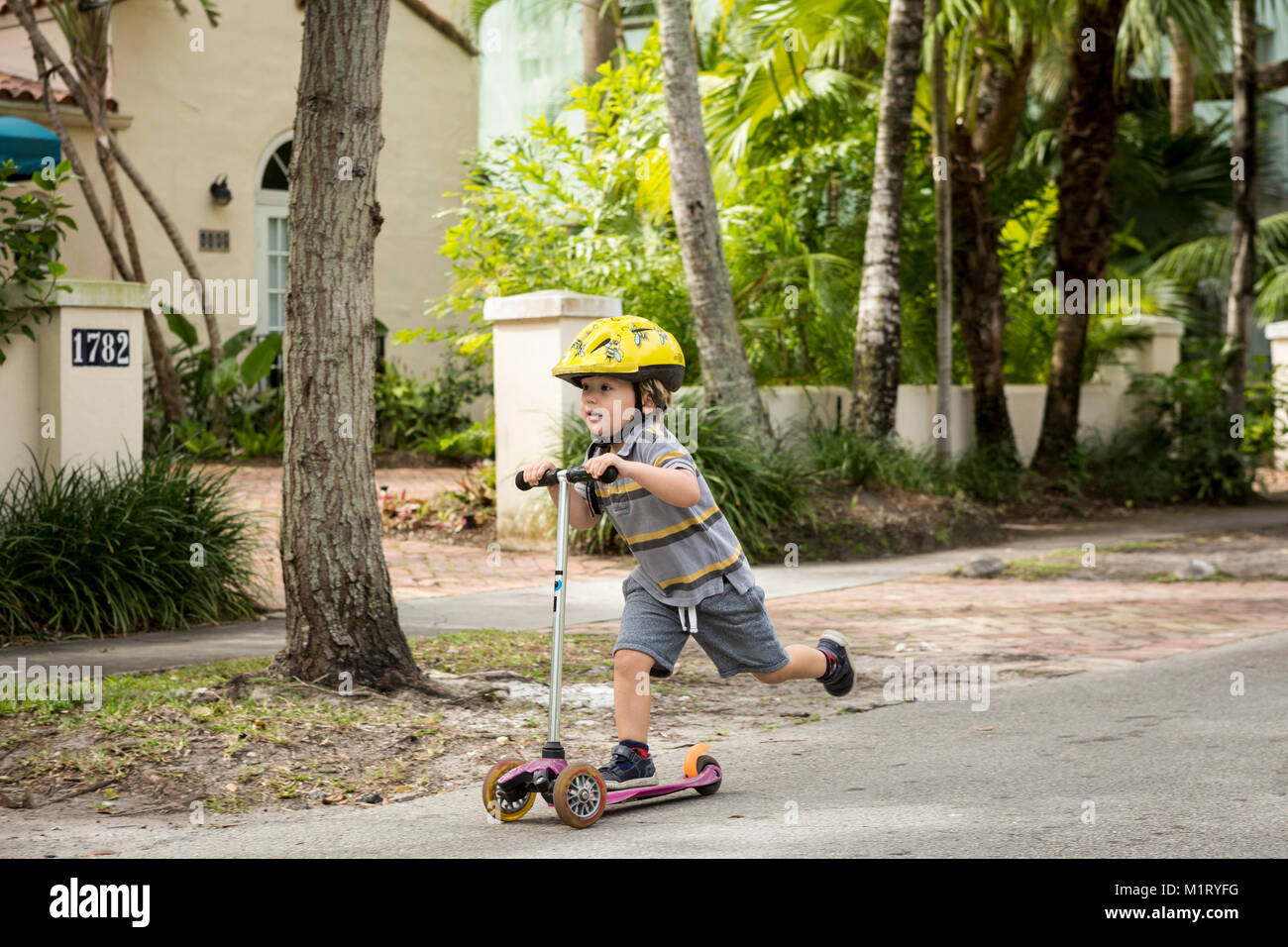 Little boy scooting down suburban street Stock Photo - Alamy