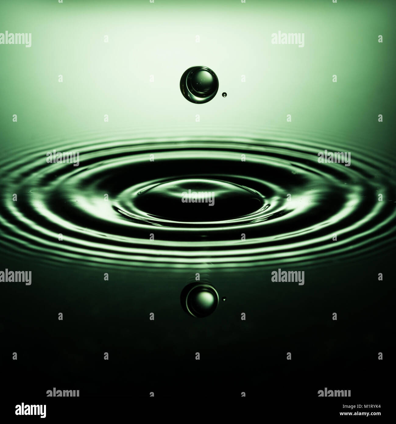 An abstract macro shot of a water drop falling into a pool of rippling ...