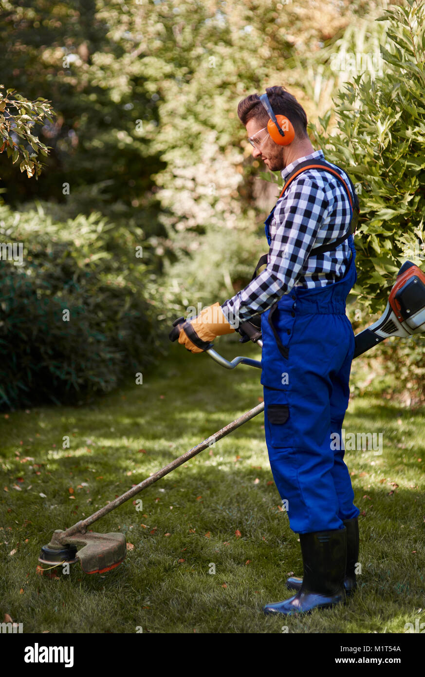 Busy man using a weedwacker at garden Stock Photo - Alamy