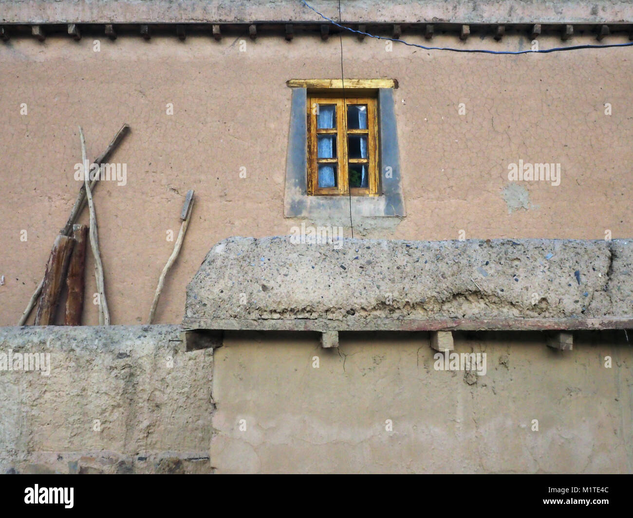 Old clay wall with a small wooden window, with yellow frames and blue ...