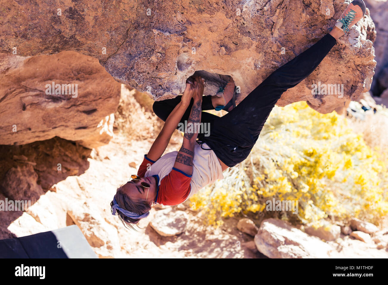 Petite asian woman rock climbing outdoors hangs from stone overhang ...