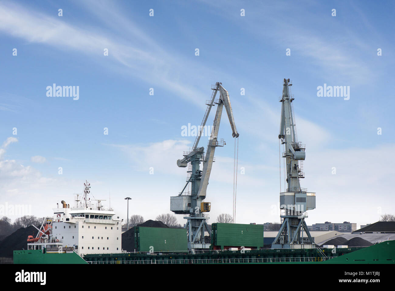 Shot of two old, rusty, grey port cranes with big hooks, lifting cargo ...