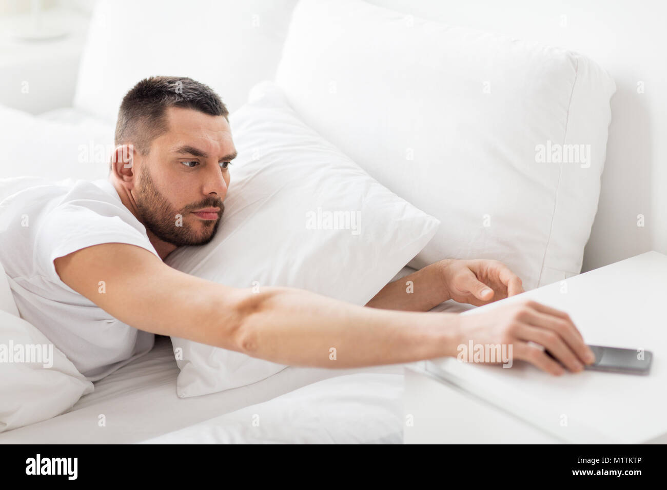 young man reaching for smartphone in bed Stock Photo - Alamy