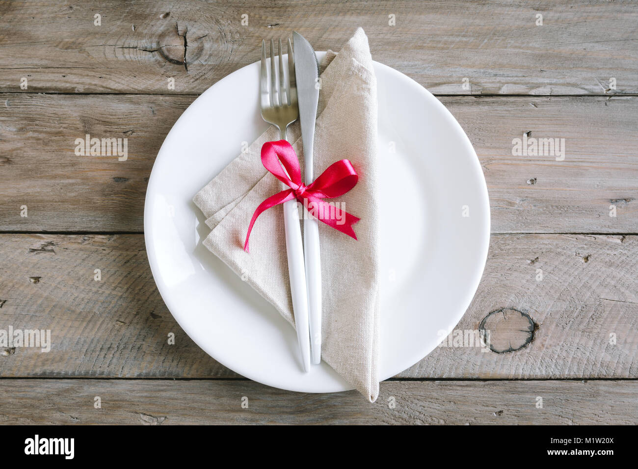 Romantic table setting with white plate, modern cutlery and red ribbon ...