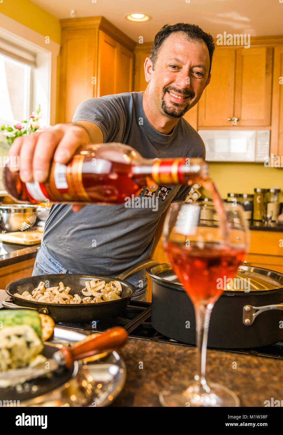 A man pouring wine into a glass in a kitchen as he cooks Stock Photo ...