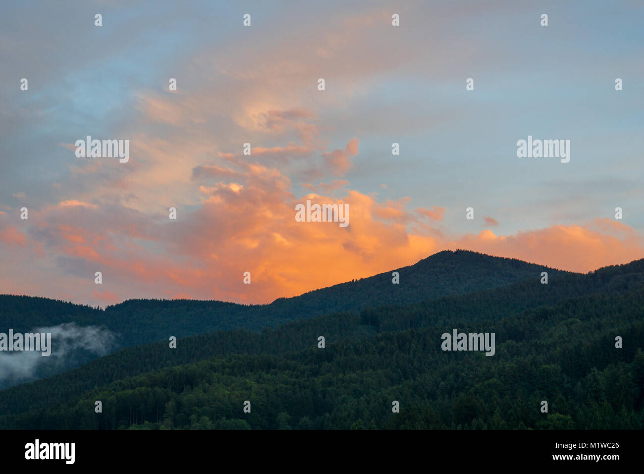 Orange dramatic sky at sunset over forest covered mountains of black ...