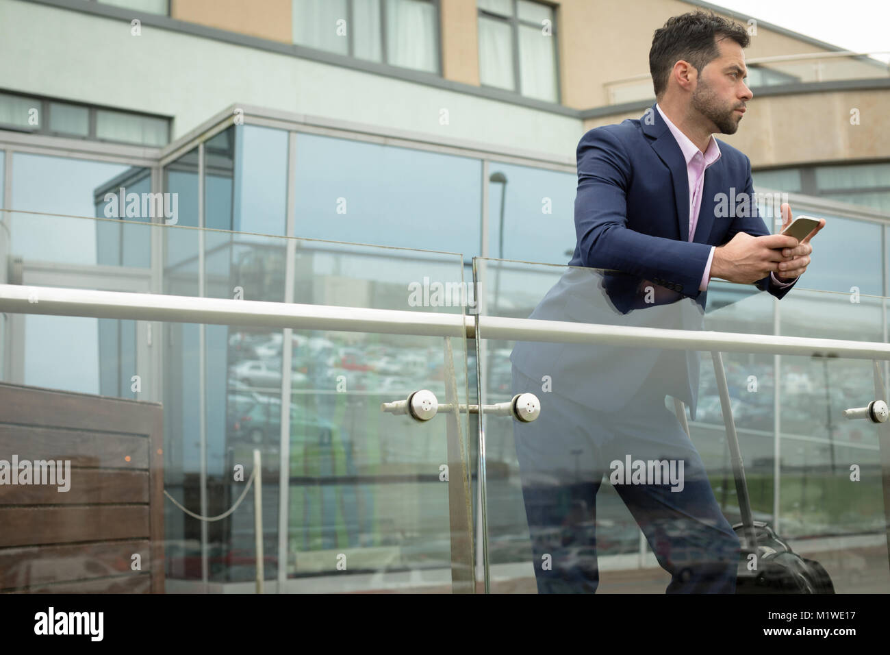 Businessman leaning on glass railing Stock Photo - Alamy