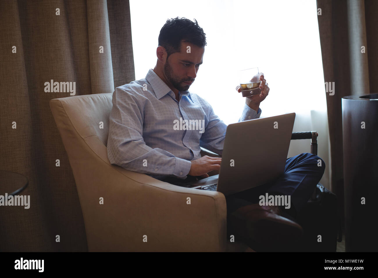 Businessman using laptop while having whisky Stock Photo - Alamy