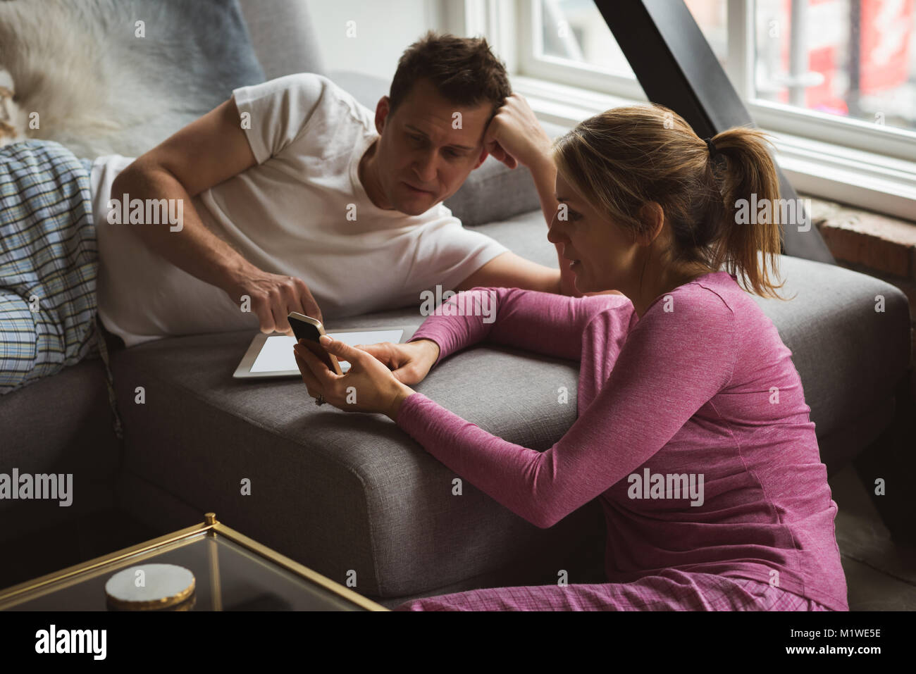 Couple using mobile phone in living room Stock Photo - Alamy