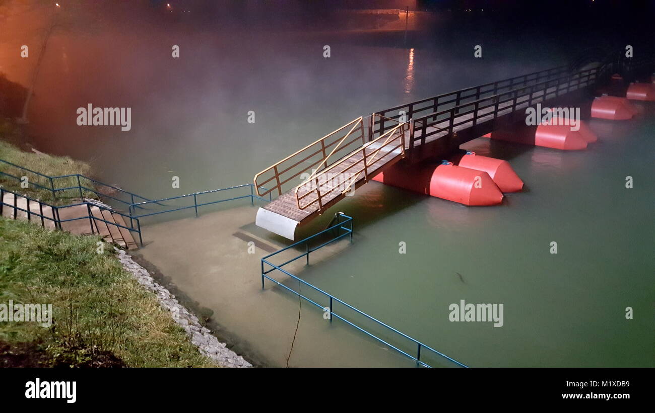 Wooden pontoon bridge surrounded with fog at night during flood, held ...