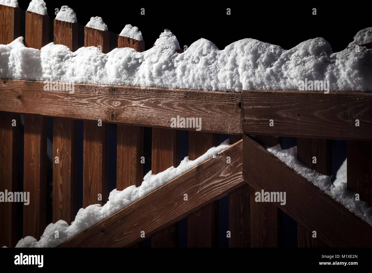 Part of the entrance wooden gate to the yard covered with snow at night ...