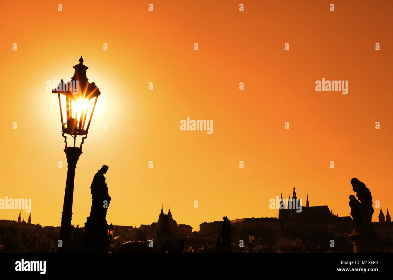 Sunset backlit silhouettes of street lamp post, statues and roofs of ...